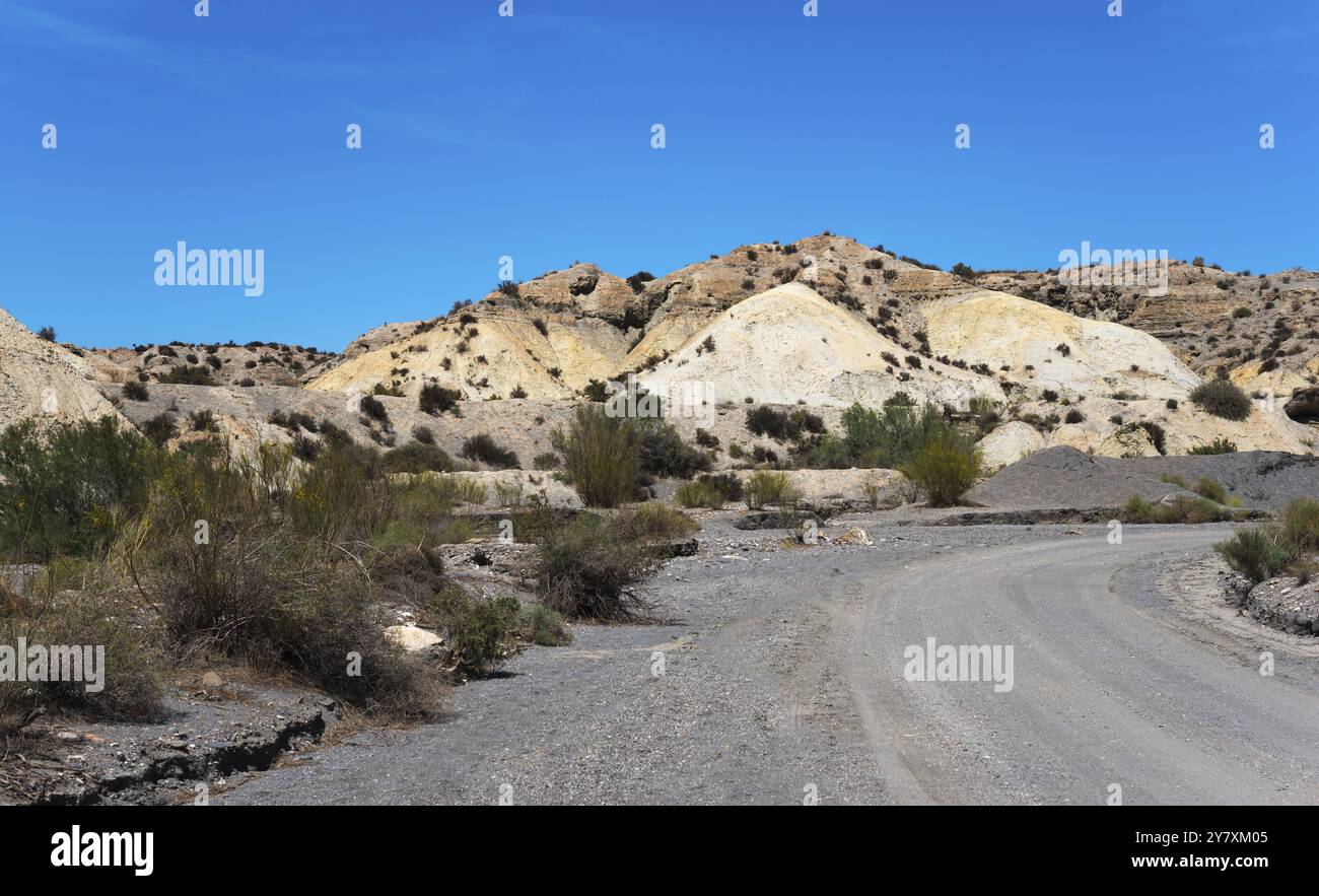 Dusty path through a dry, rocky desert landscape under a clear blue sky ...