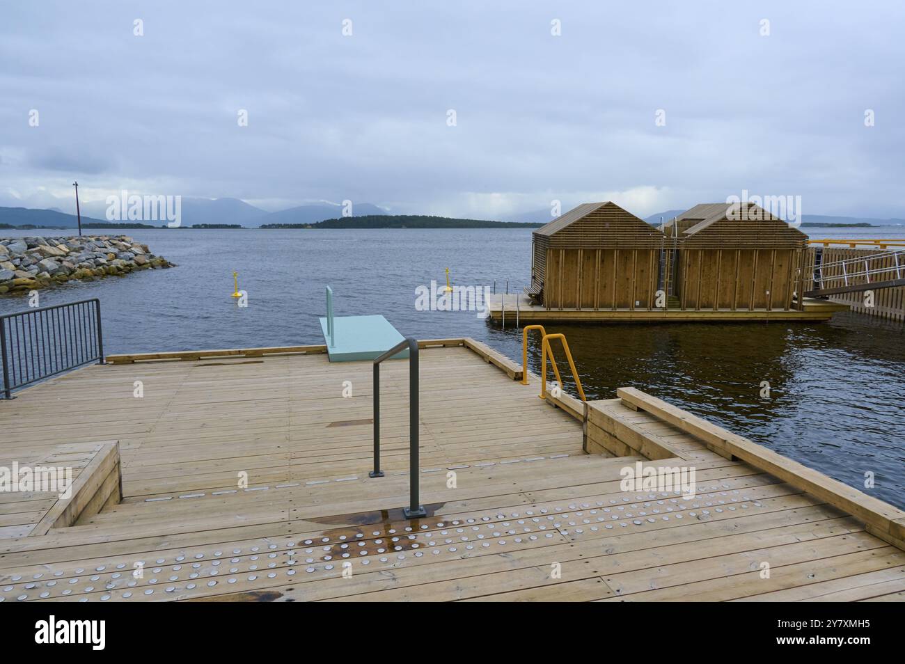 Outdoor sea pool by the fjord with small wooden sauna huts, overcast ...