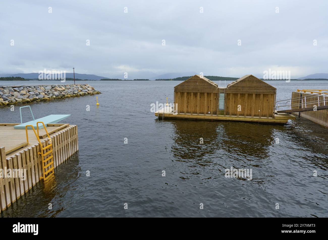 Outdoor sea pool by the fjord with small wooden sauna huts, overcast ...