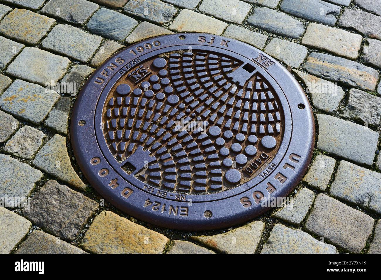 Round manhole cover with geometric pattern on cobblestones, Bergen ...