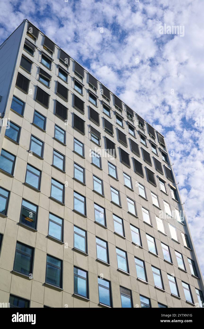 A modern skyscraper with many glass windows stands in front of a cloudy ...