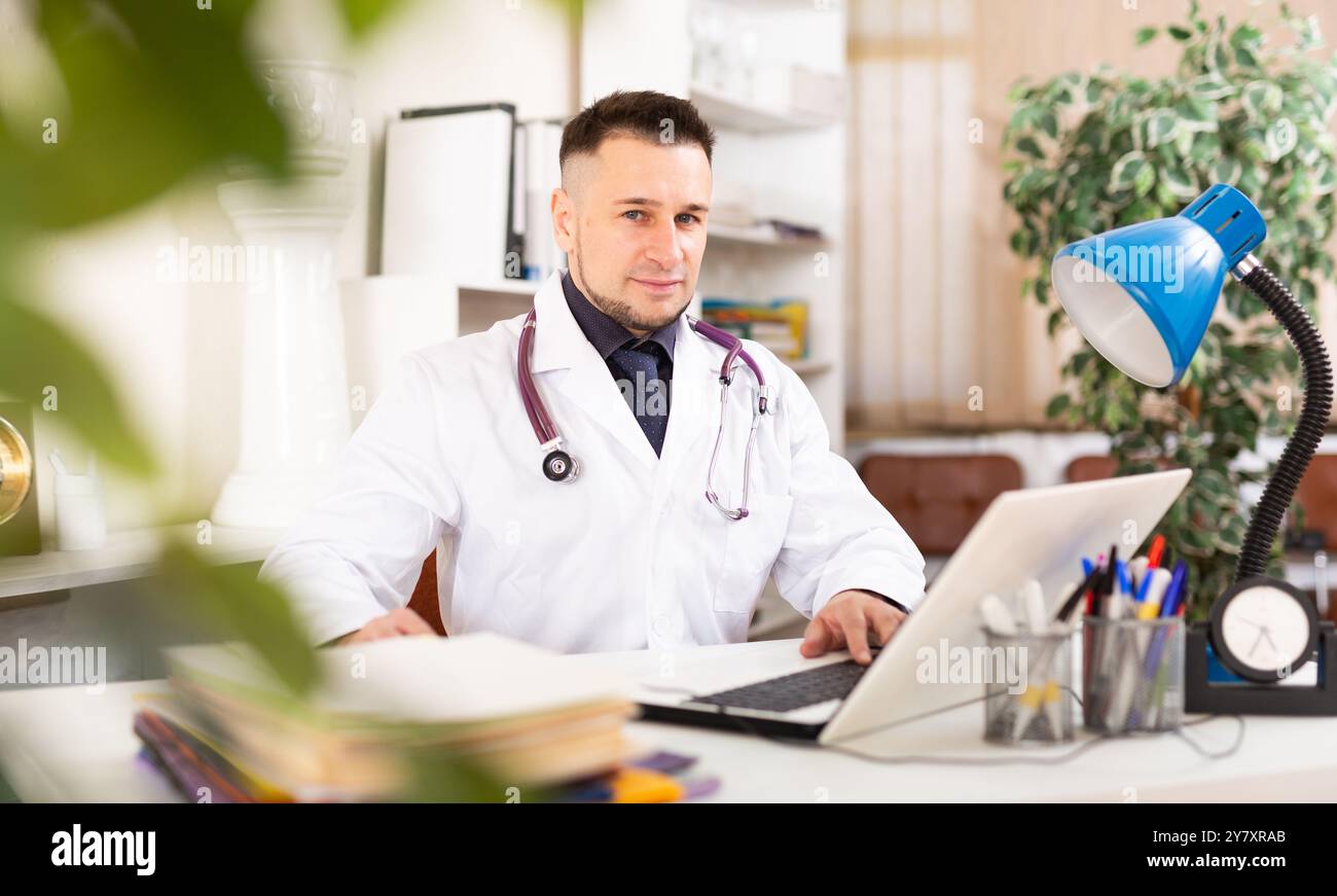Positive man doctor therapist sitting in office at workplace and ...