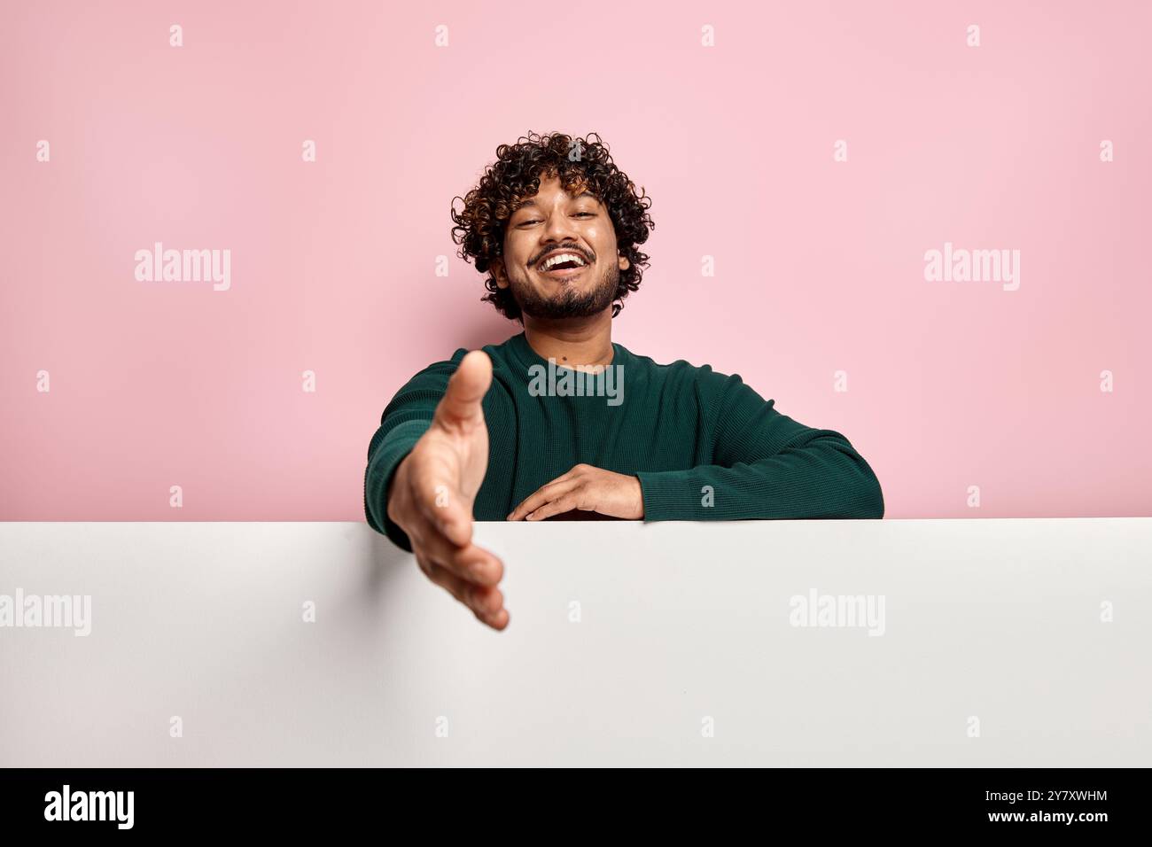 Happy young Indian man stretching out hand for shaking against pink ...