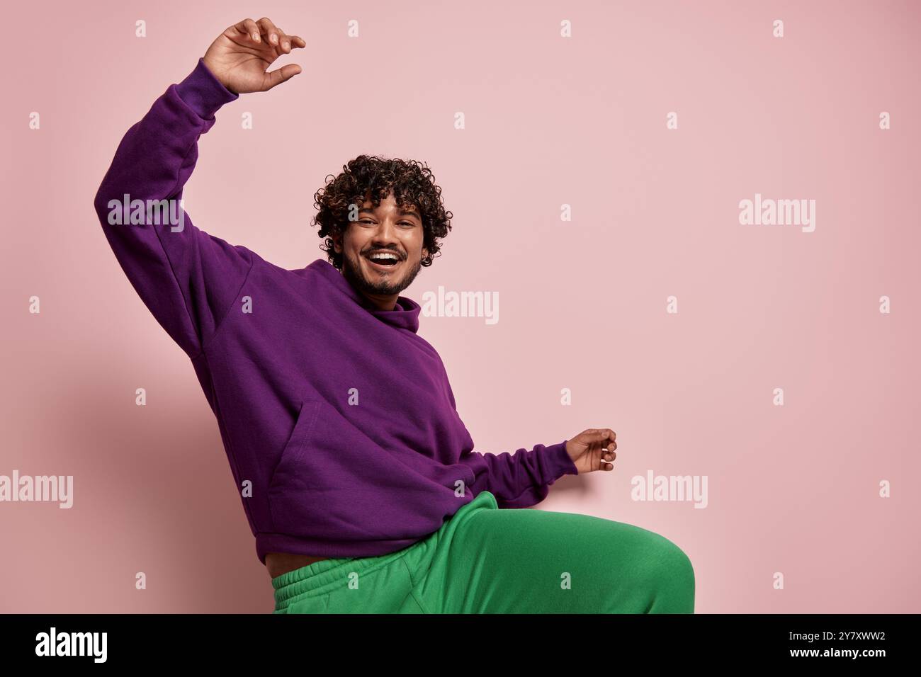 Excited young Indian man dancing and smiling against pink background ...