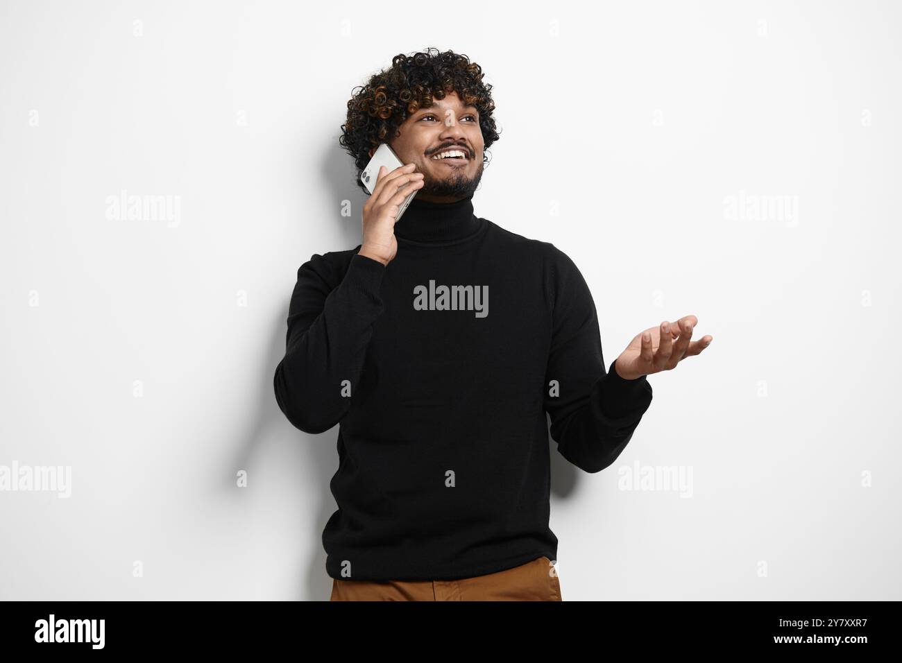 Handsome Indian man talking on phone and smiling while standing against ...