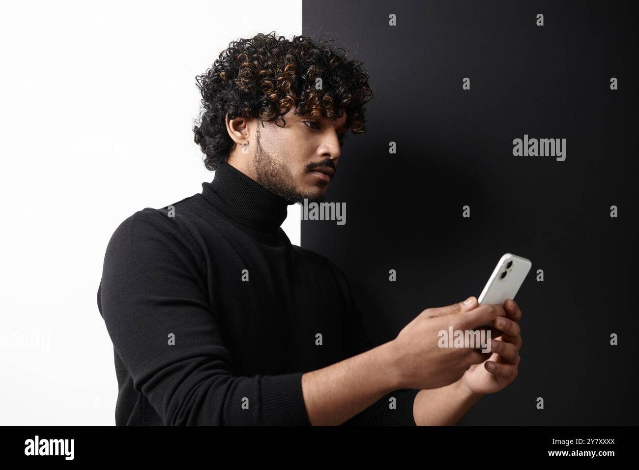 Confident Indian man using smart phone while standing against black and ...