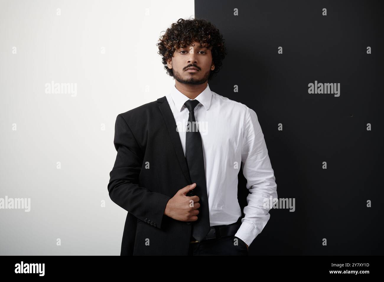 Handsome Indian man holding jacket on one shoulder against black and ...