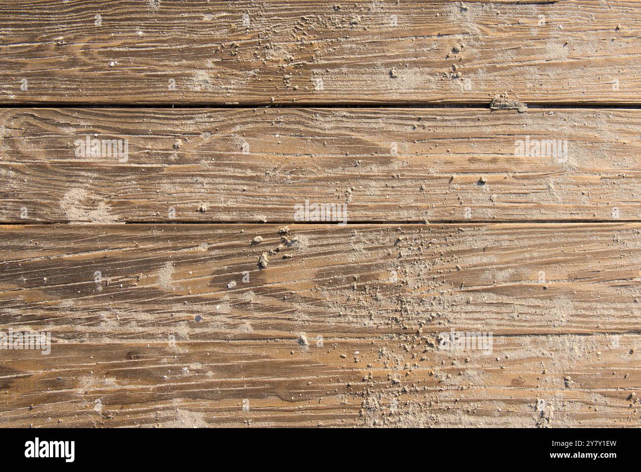A close-up of weathered wooden planks with scattered sand. The texture highlights the natural ...