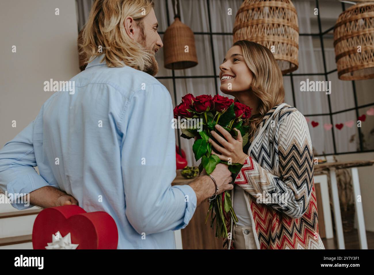Young smiling man giving a red roses bouquet to his surprised ...