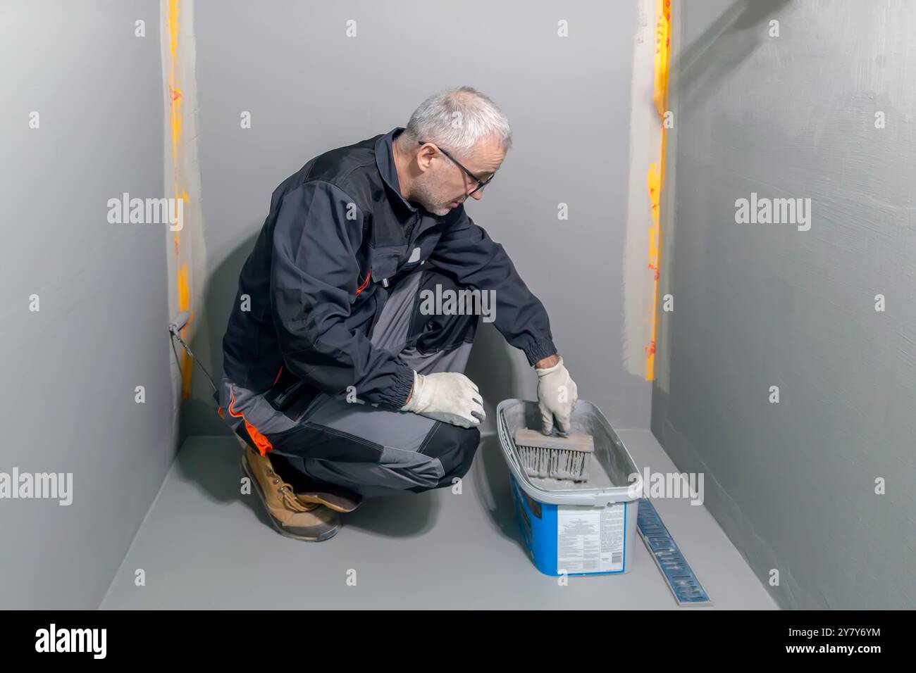 A builder worker applying waterproofing paint to the bathroom wall and ...