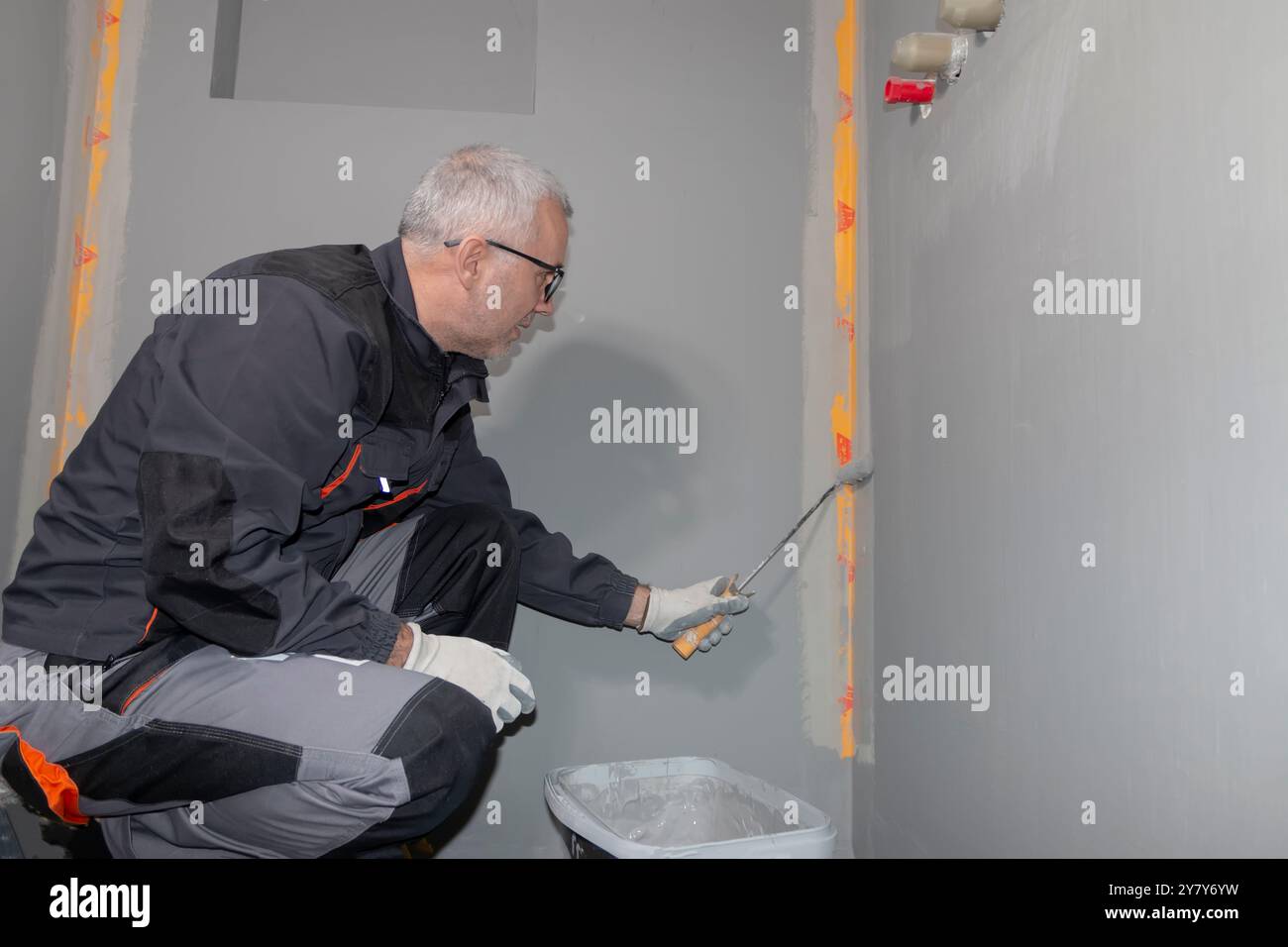A builder worker applying waterproofing paint to the bathroom wall and ...