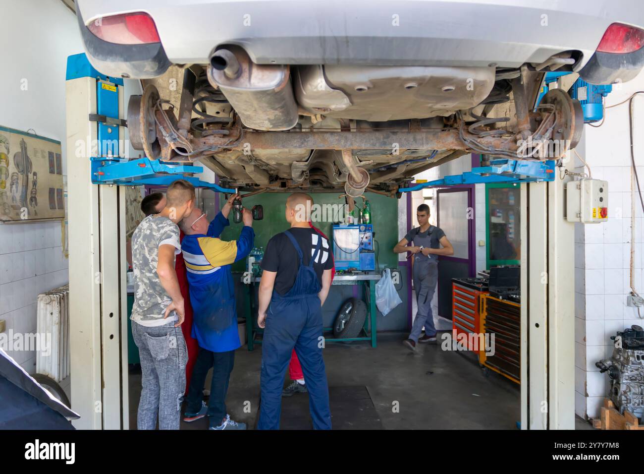 Senior experienced teacher standing underneath car on hydraulic ramp ...