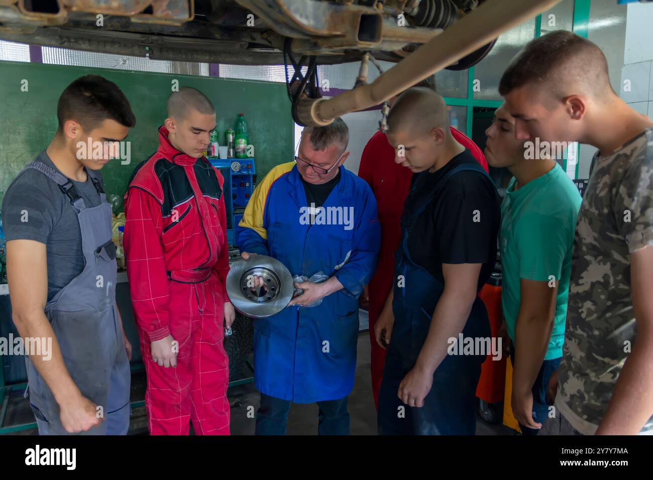 Mature experienced teacher standing underneath car on hydraulic ramp ...
