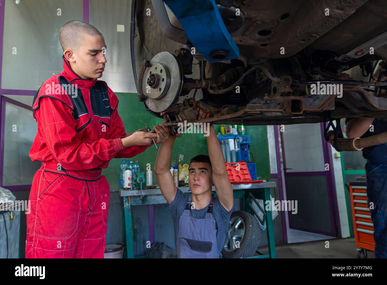 Young auto mechanics underneath car on hydraulic ramp on working in ...
