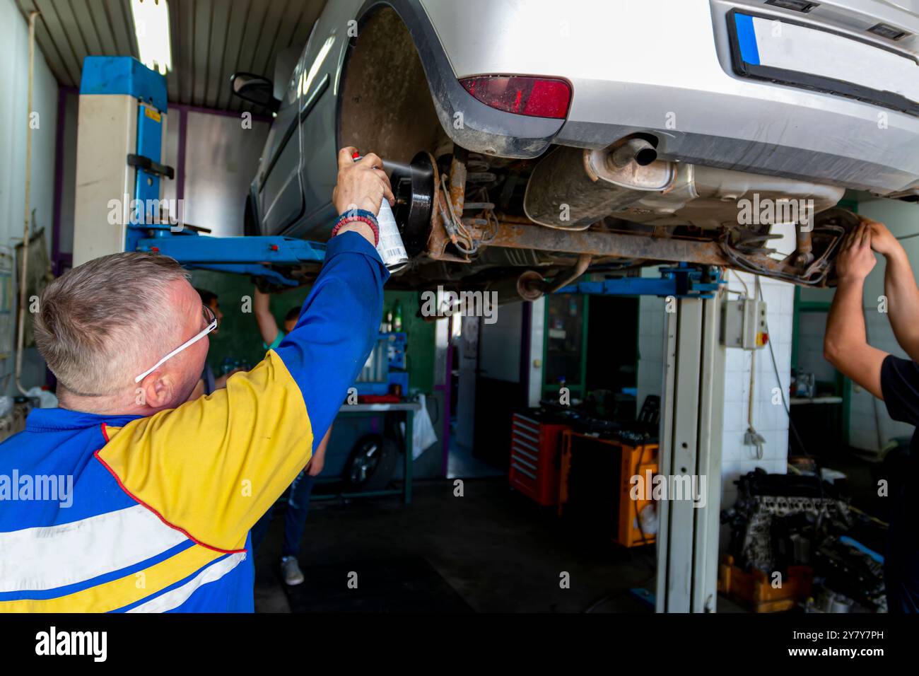 Mature experienced teacher standing underneath car on hydraulic ramp ...