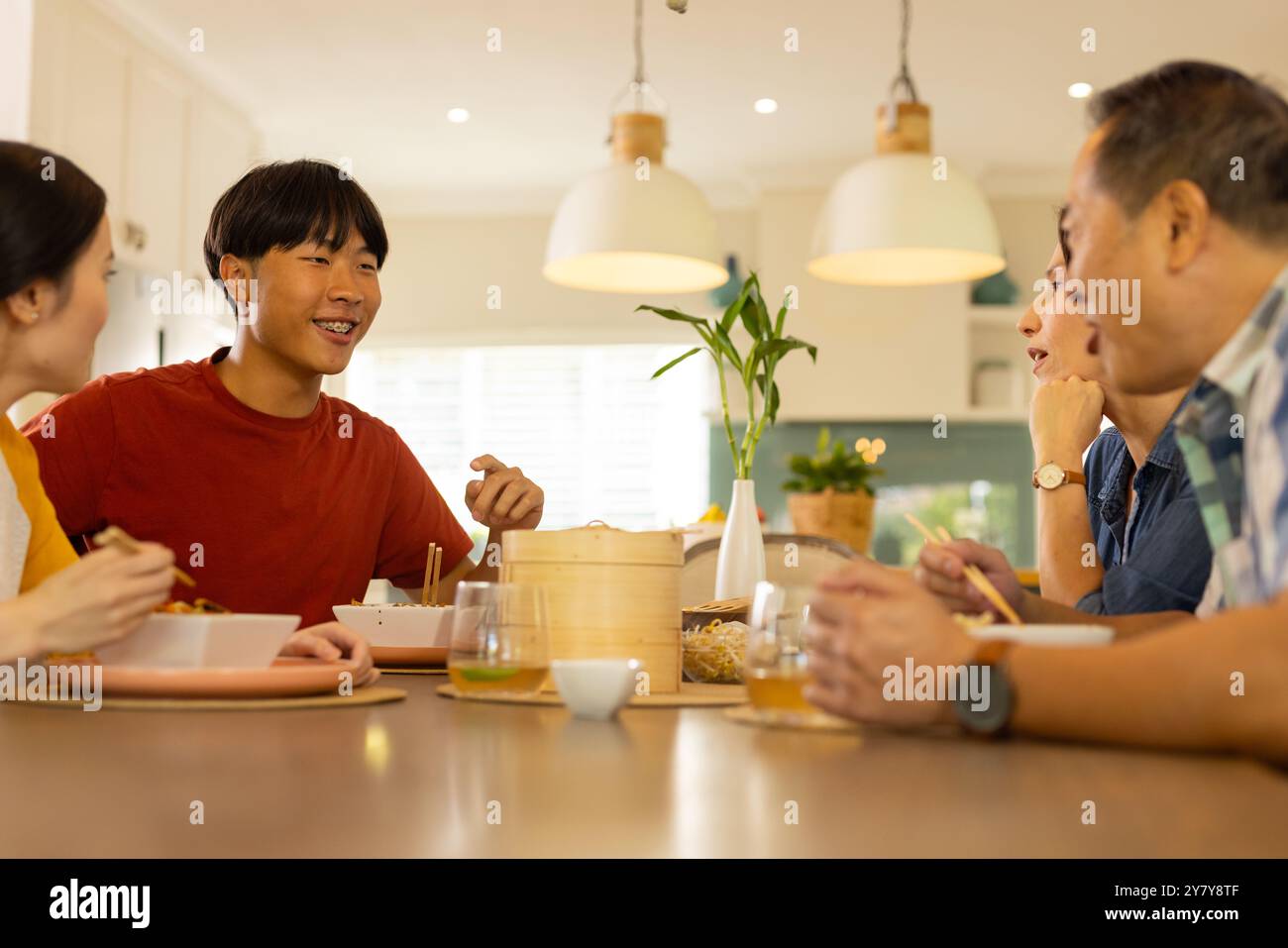 At home, asian family enjoying meal together, talking and smiling ...