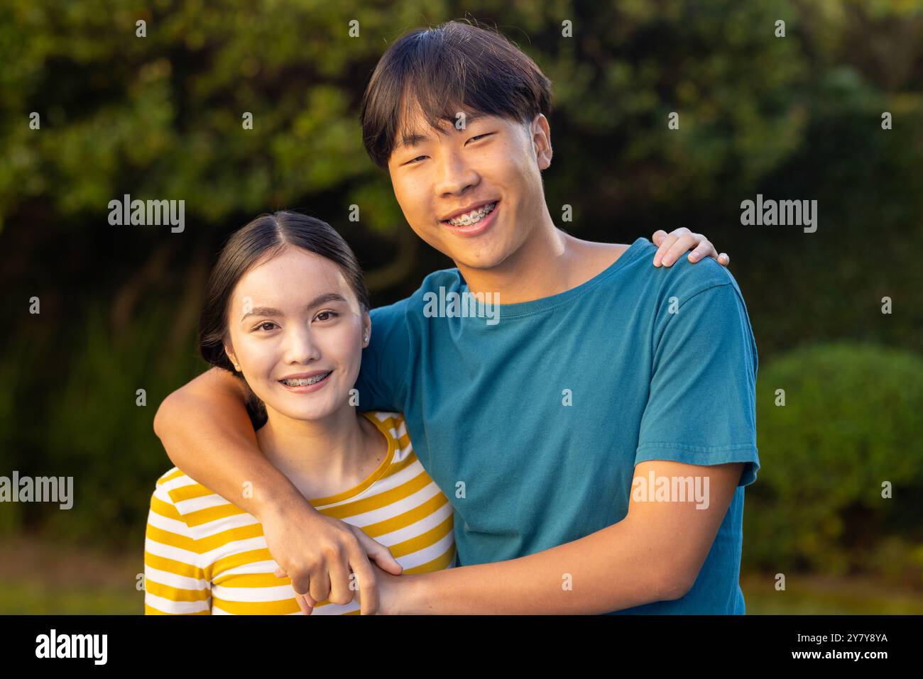 Smiling young asian brother and sister hugging outdoors, enjoying time ...