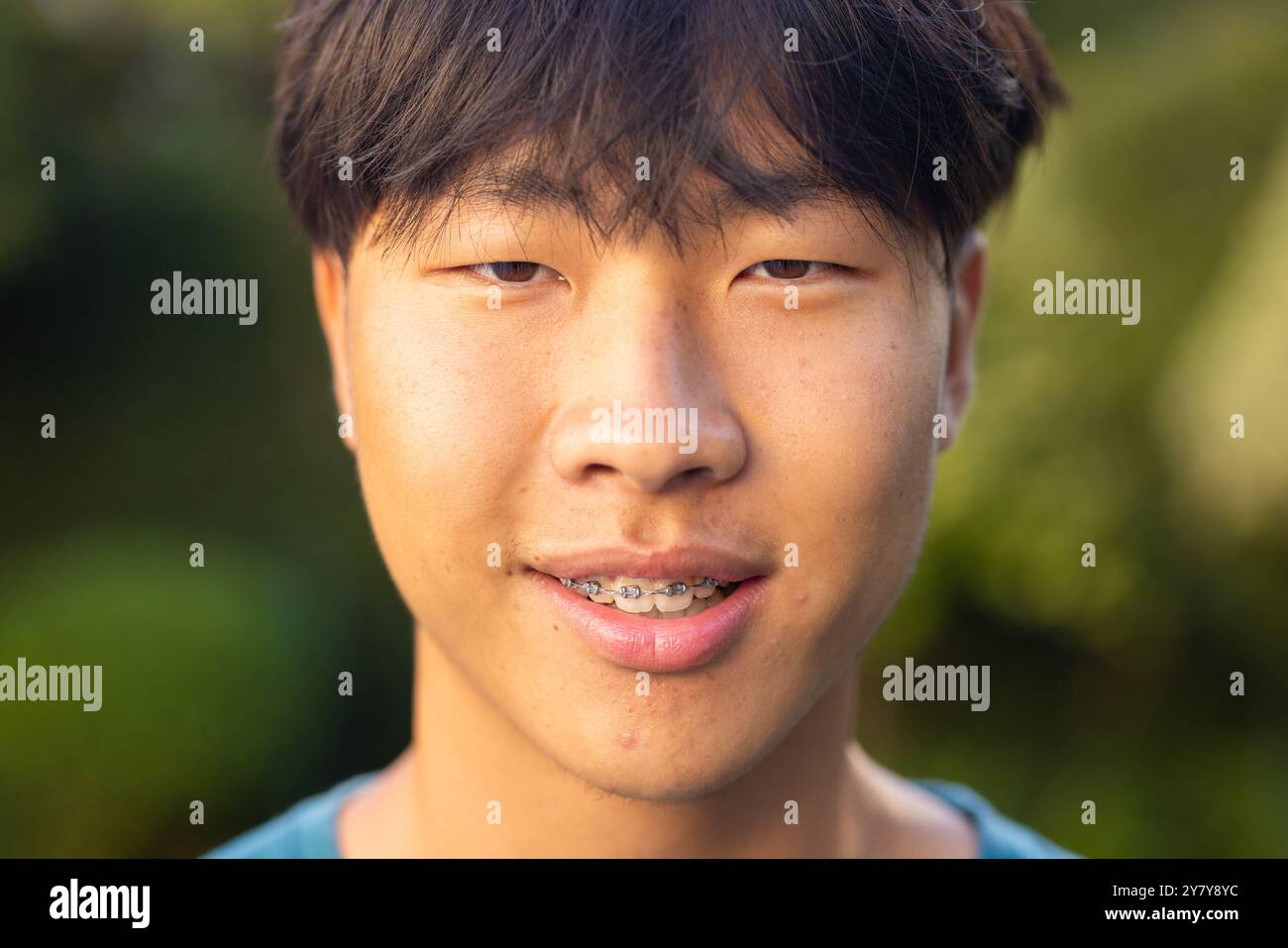 Smiling teenage asian boy with braces enjoying outdoor time in natural ...