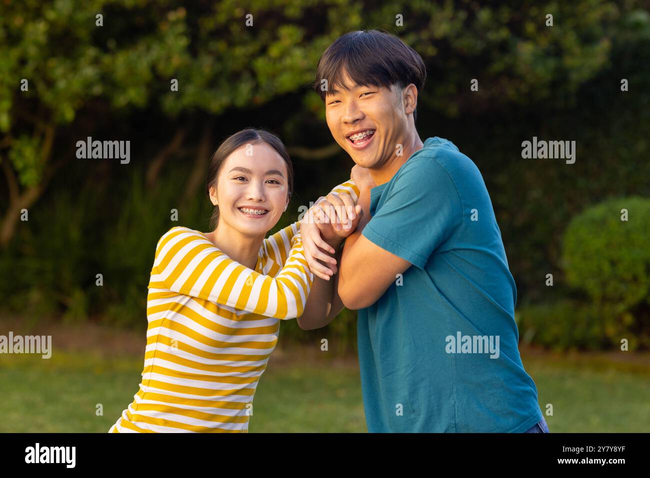 Smiling young asian brother and sister playfully holding hands outdoors ...