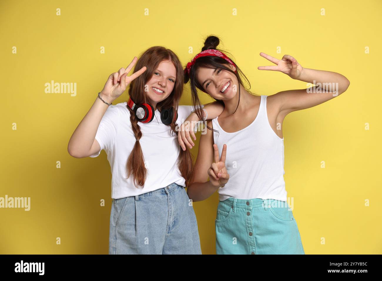 Happy teenage girls showing peace signs on yellow background Stock ...