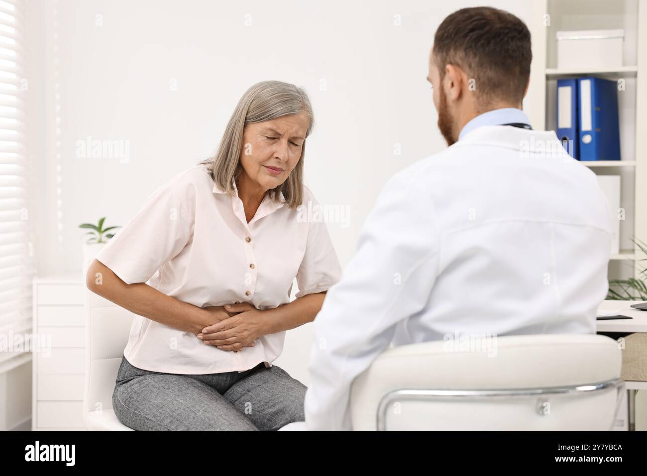 Doctor consulting senior patient with stomach pain in clinic, back view ...