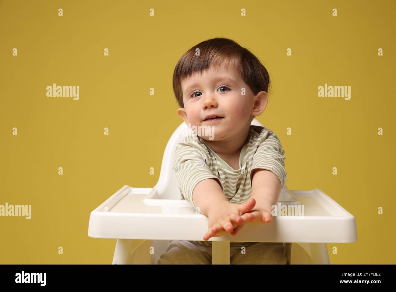 Cute little kid sitting in high chair on yellow background Stock Photo ...