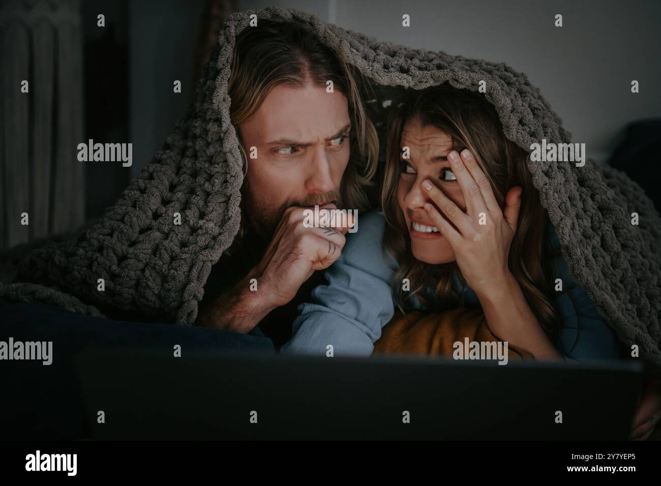 Scared young couple covering with blanket and watching horror movie on ...