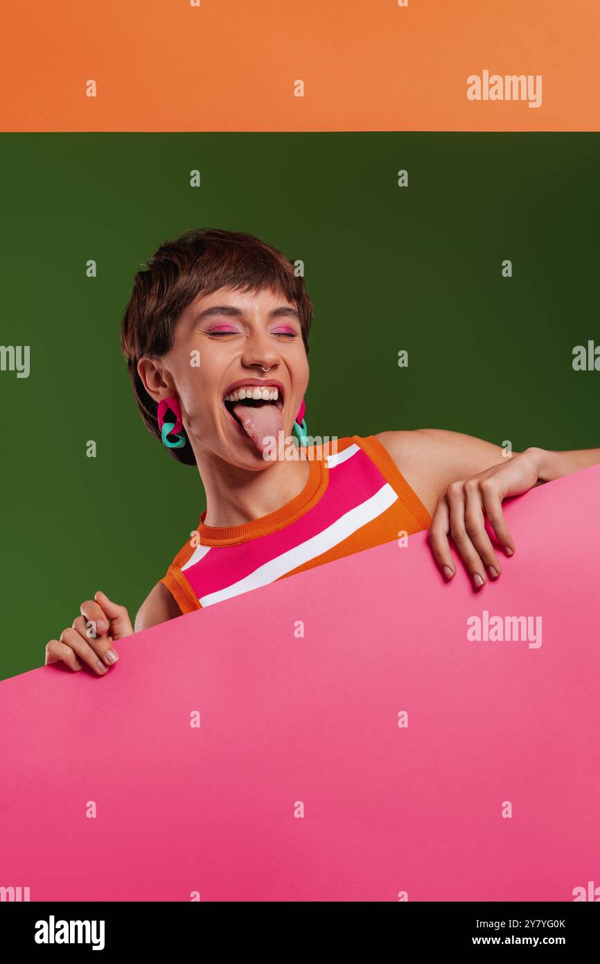 Playful young woman sticking out tongue while looking out of the colorful banners Stock Photo ...