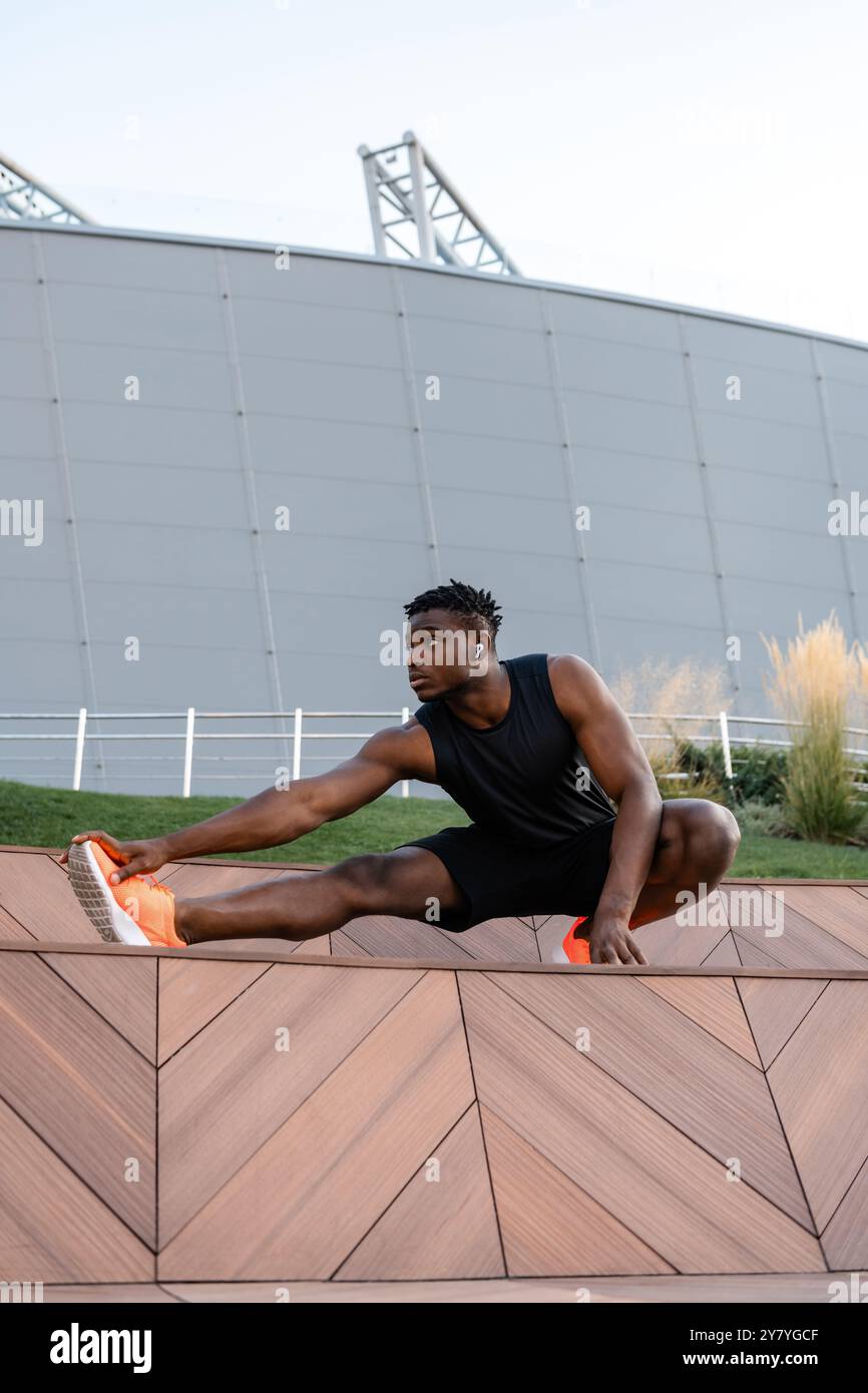 Concentrated young African man in sportswear doing stretching exercises ...