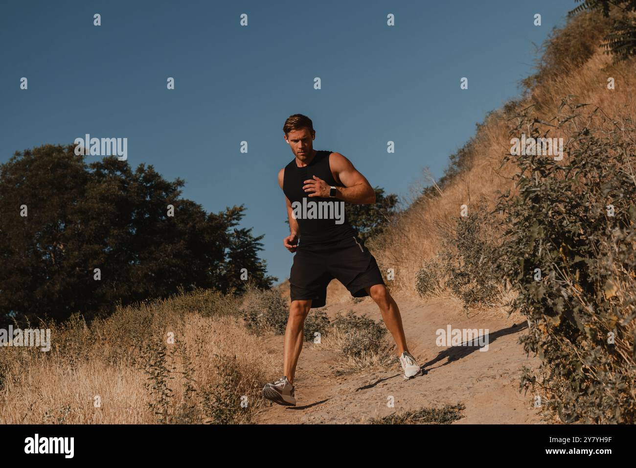 Confident male athlete in sports clothing running down the hill ...