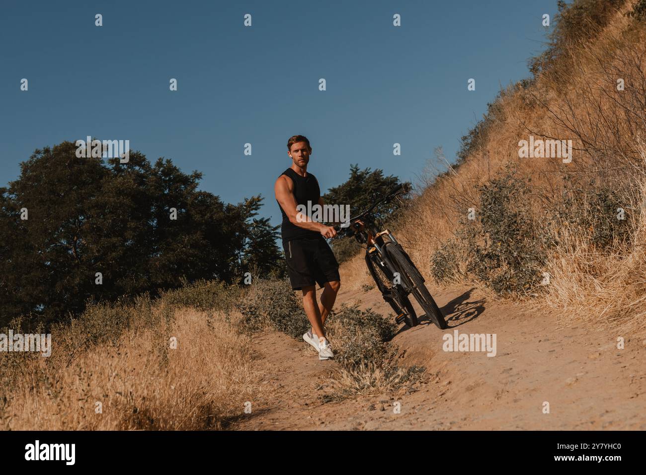 Confident young man in sports clothing pulling his bicycle down by ...