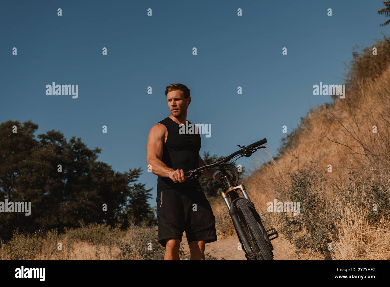 Confident young man in sports clothing pulling his bicycle down by ...