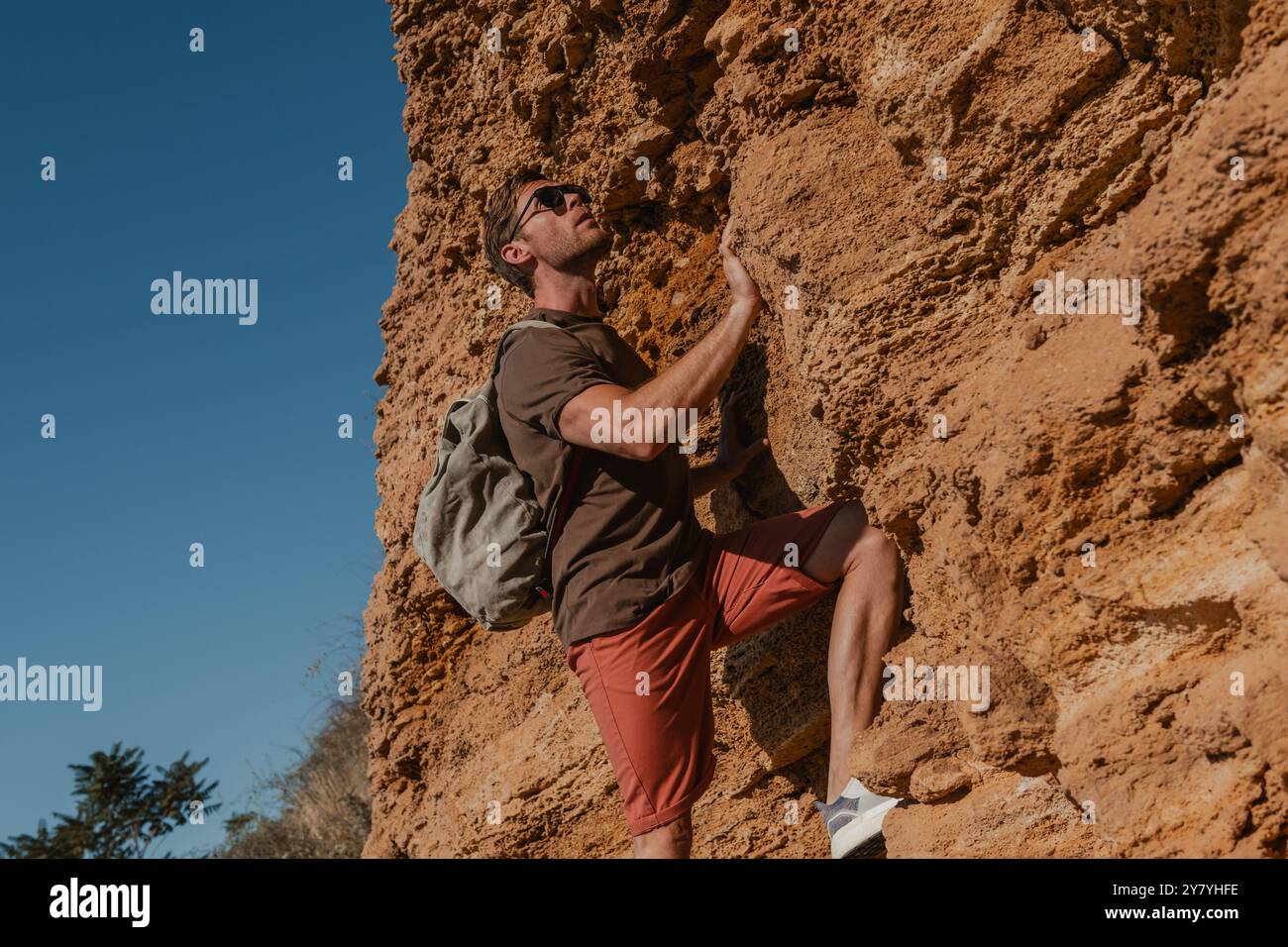 Confident male adventurer with backpack holding on grip while climbing ...
