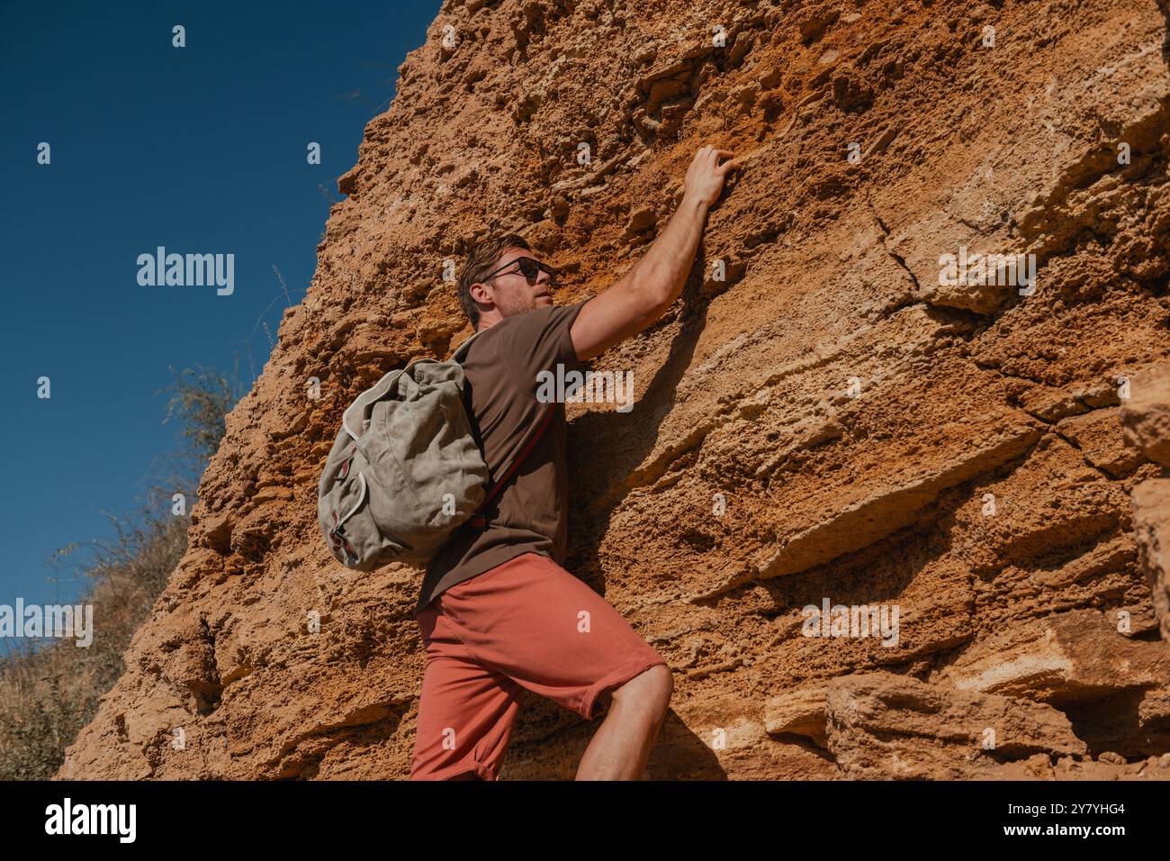 Strong male adventurer with backpack holding on grip while climbing the ...