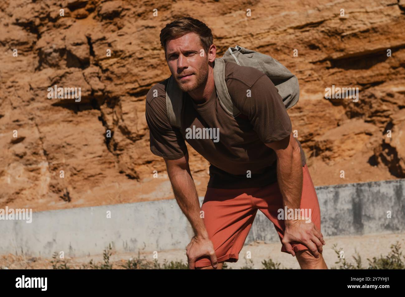 Tired adventurer with backpack holding hands on knees while resting ...