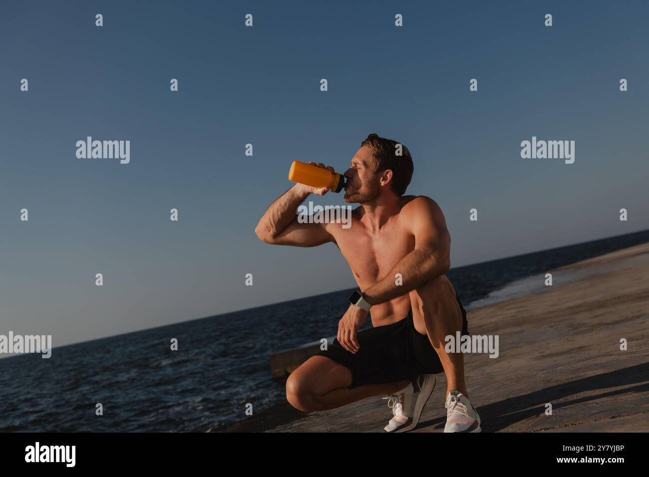 Confident male athlete drinking water while resting after morning ...