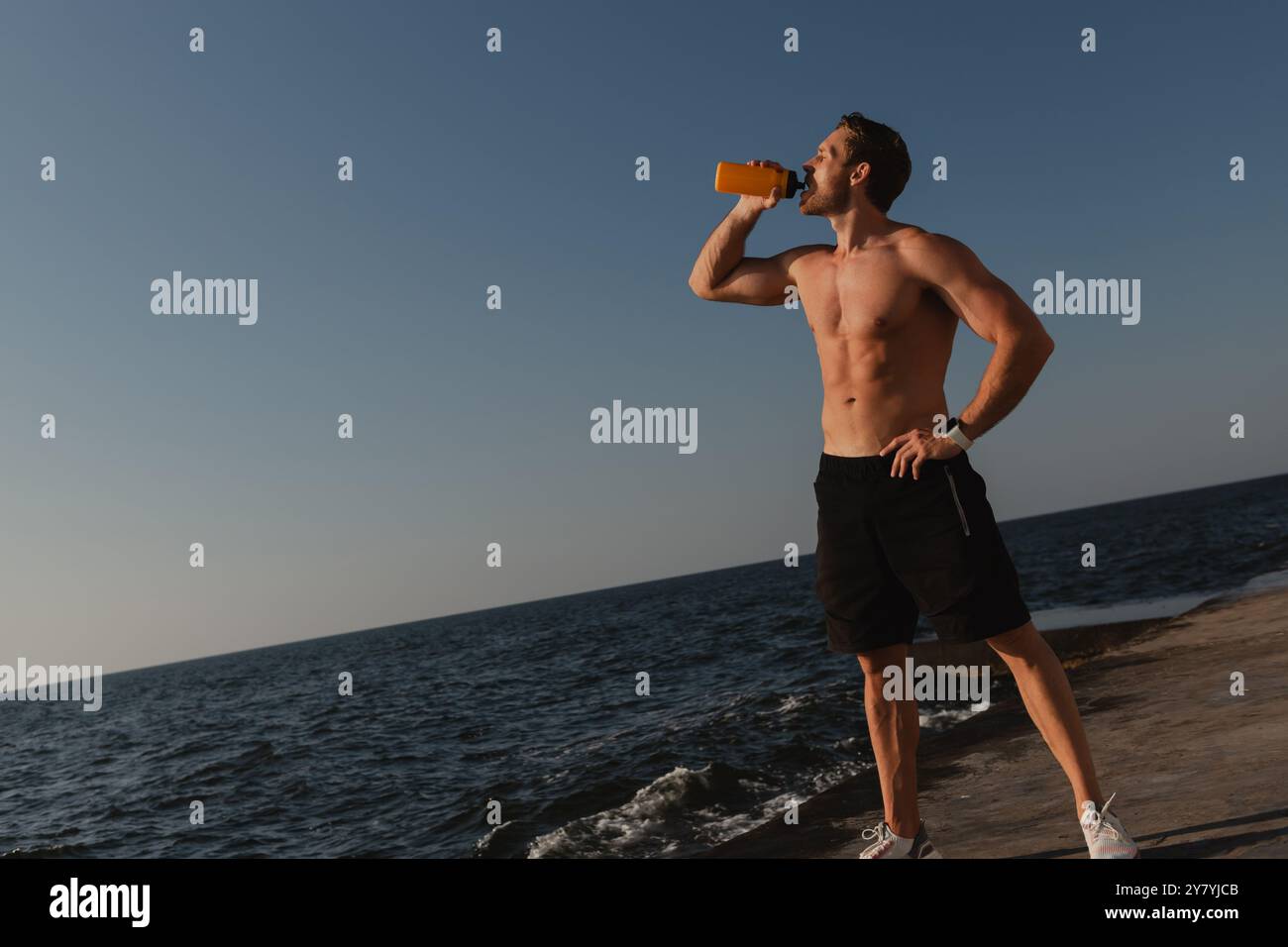Confident male athlete drinking water while relaxing after sport ...