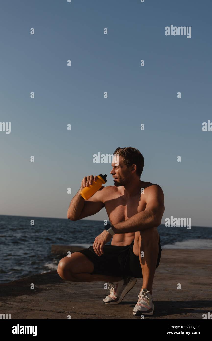 Confident male athlete drinking water while relaxing after morning ...