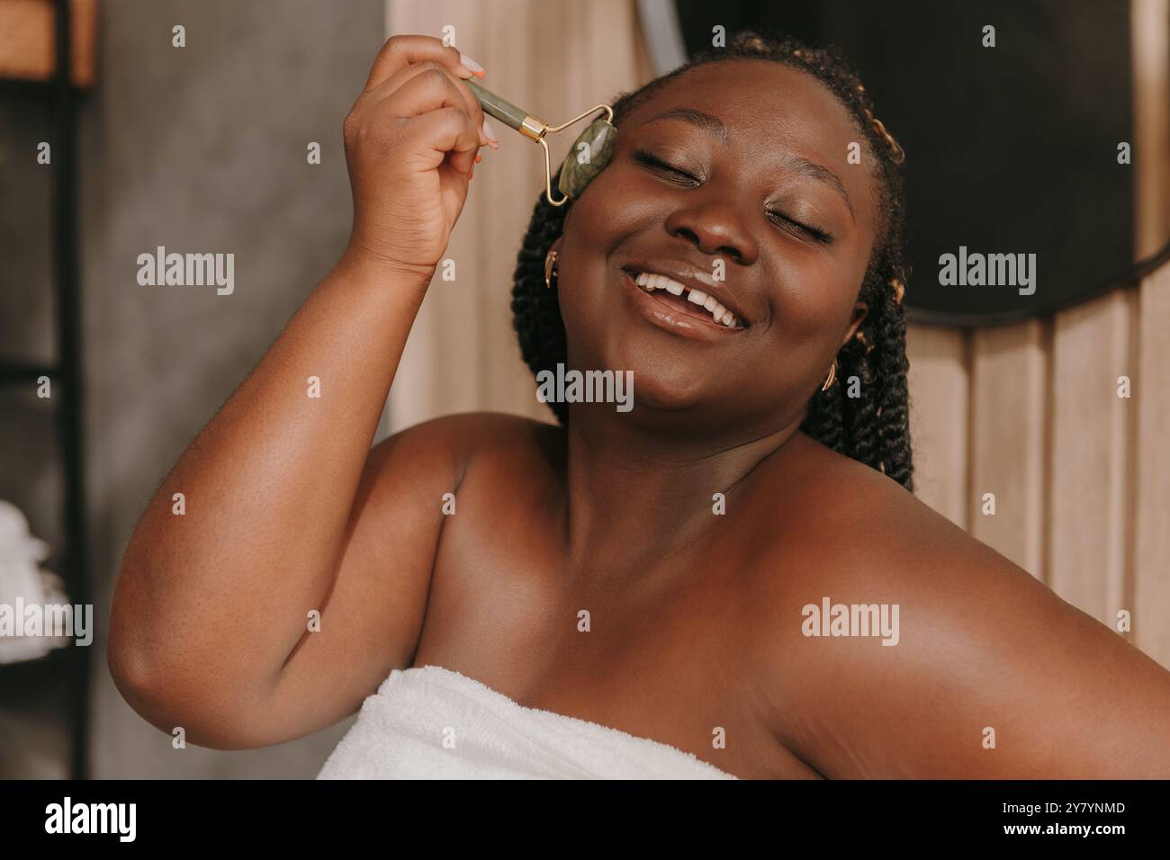Beautiful plus size African woman covered in towel massaging face with ...