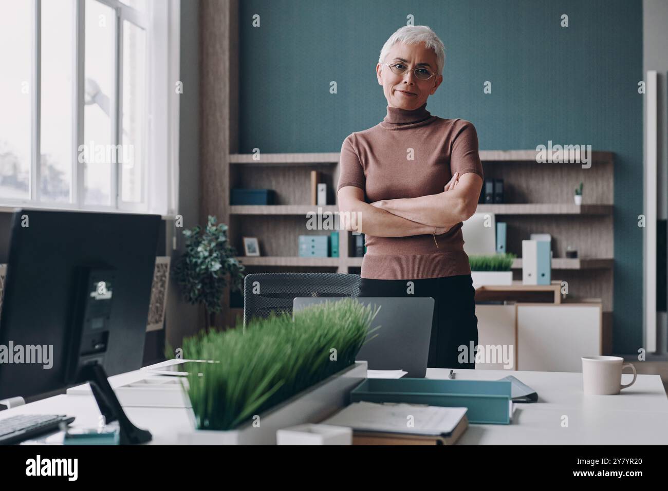 Senior businesswoman keeping arms crossed while standing near her ...