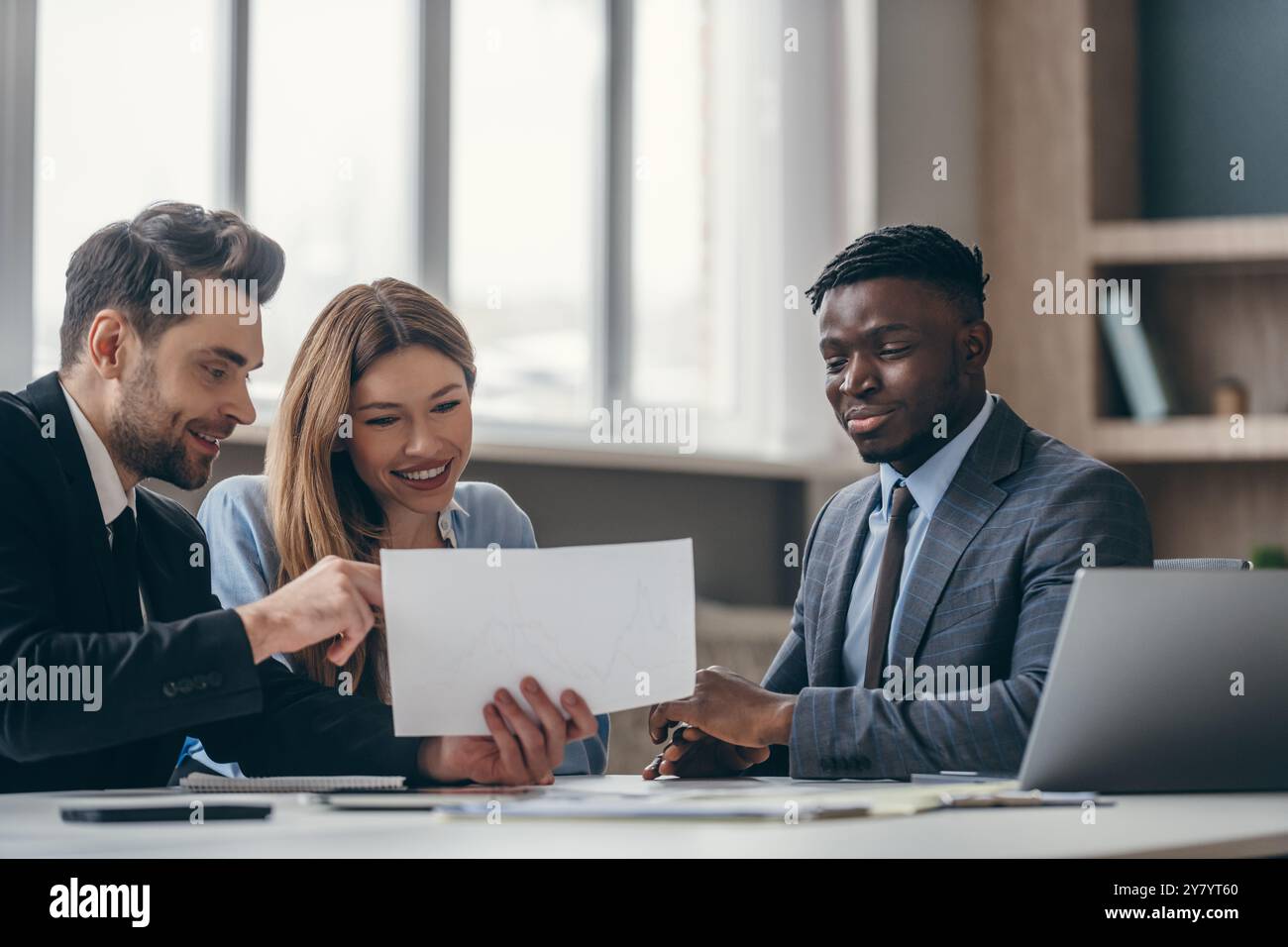 Smiling young couple sitting at the office desk and examining papers ...