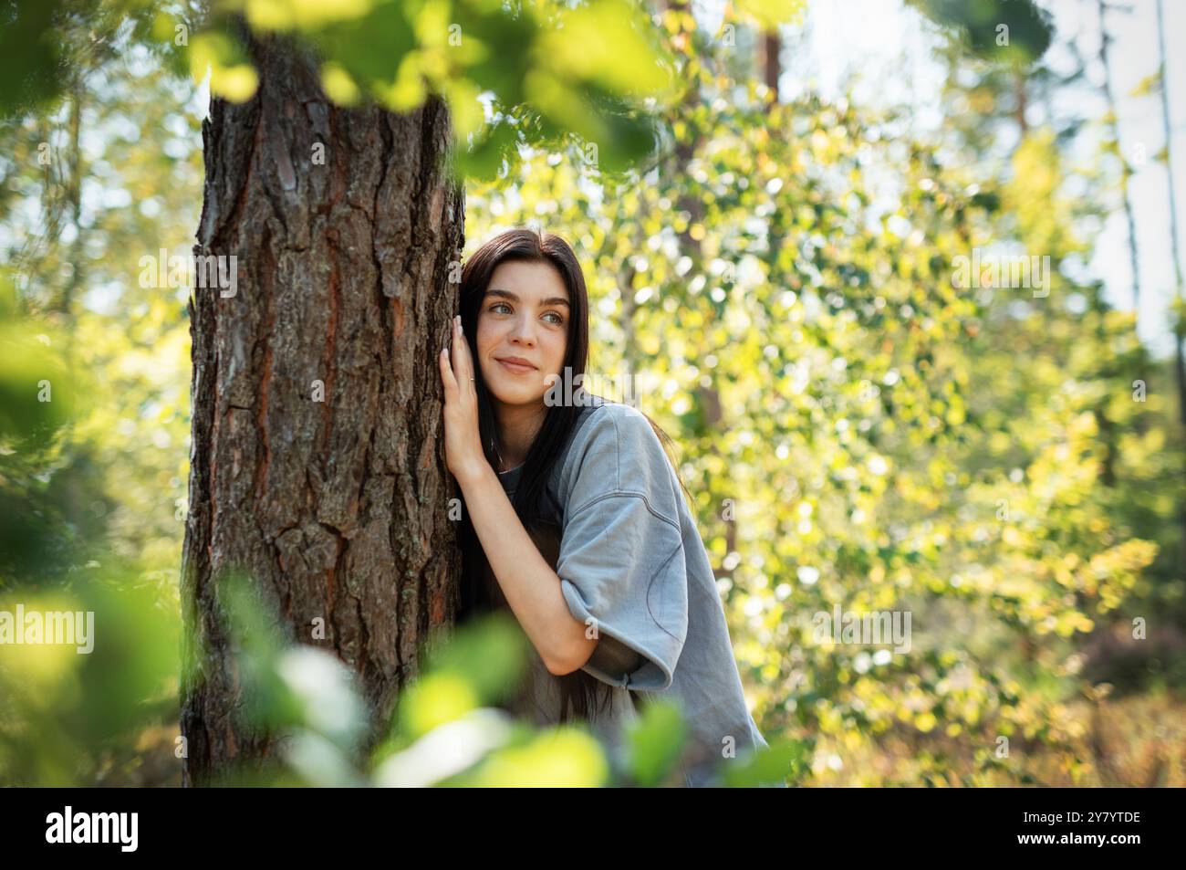 A young girl hugs a tree in the forest. Hugging and touching trees to ...