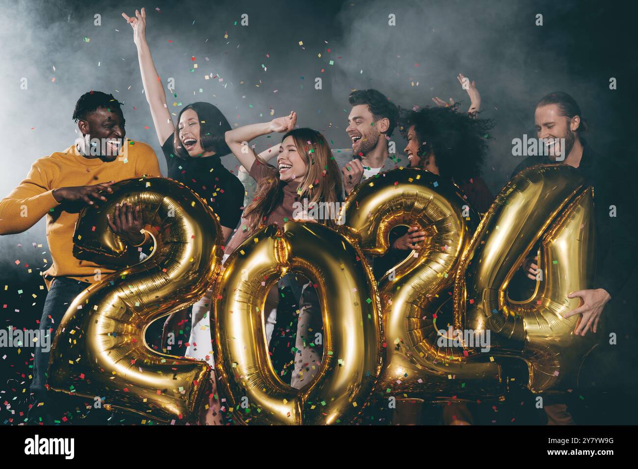 Group of joyful young people celebrating 2024 New Year while throwing ...