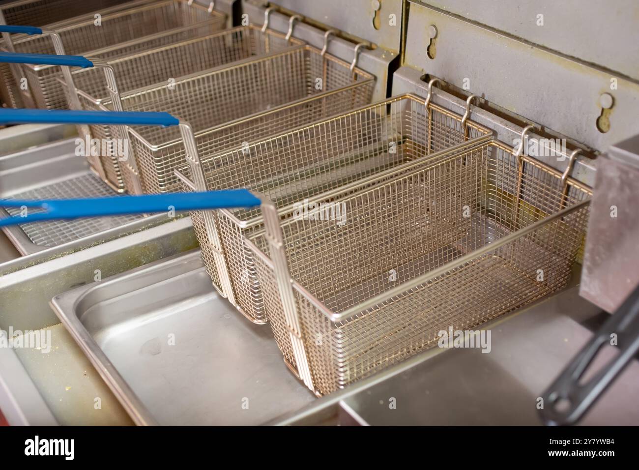 A view of a row of empty fry baskets hanging on a deep fryer appliance ...