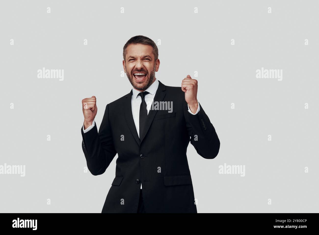 Charming young man in full suit cheering while standing against grey ...