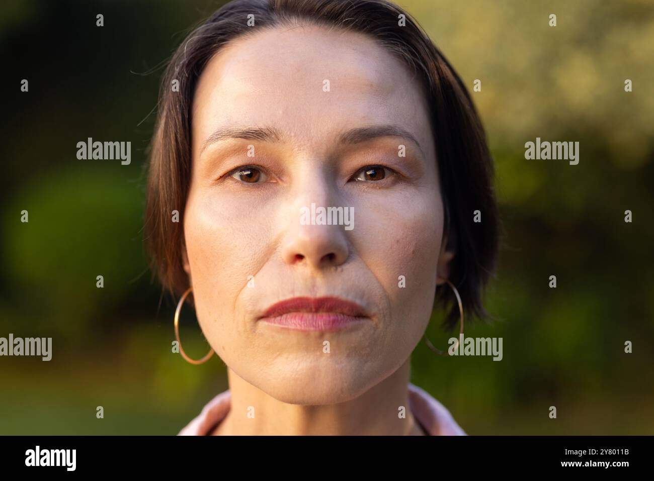 Close-up portrait of middle-aged woman with short hair and hoop earrings, looking serious ...