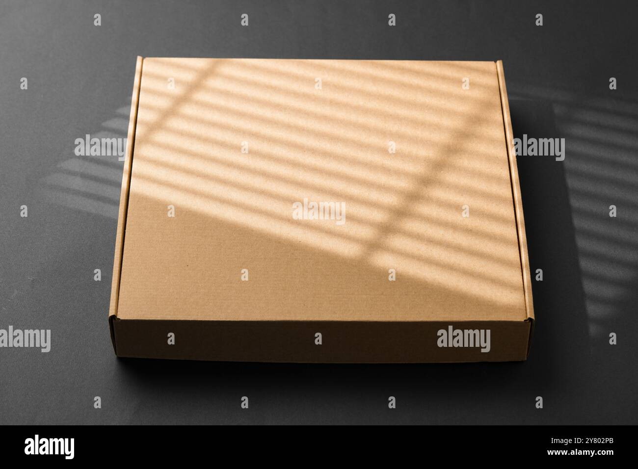 A cardboard box casting shadows on a dark surface in a striped light ...