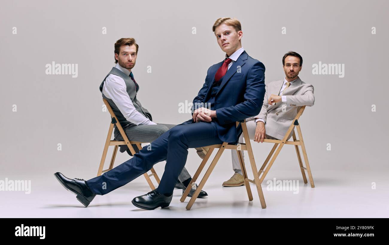 Group of young men sitting on chairs in relaxed pose. They exude ...