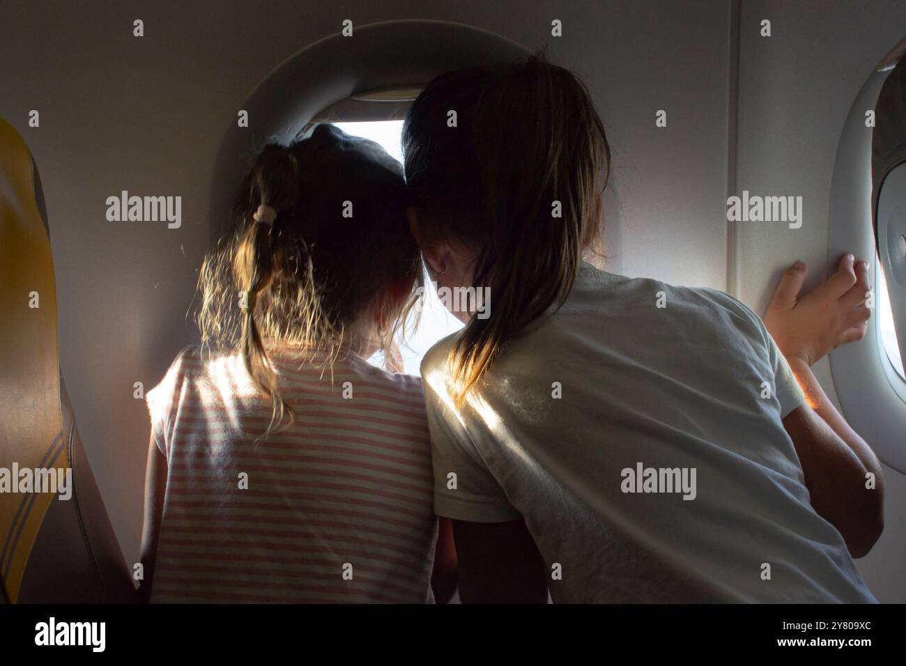 Two excited sisters looking out the airplane window during their first ...
