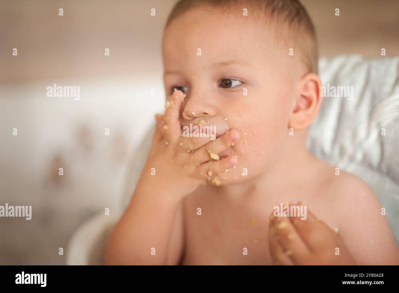 A young child indulges in a snack, using both hands to explore the food ...